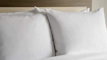 Uma cama com roupa de cama e almofadas brancas.