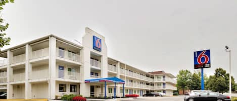 Um motel com placa indicando o número '6', várias varandas e uma entrada com a palavra 'Welcome'.