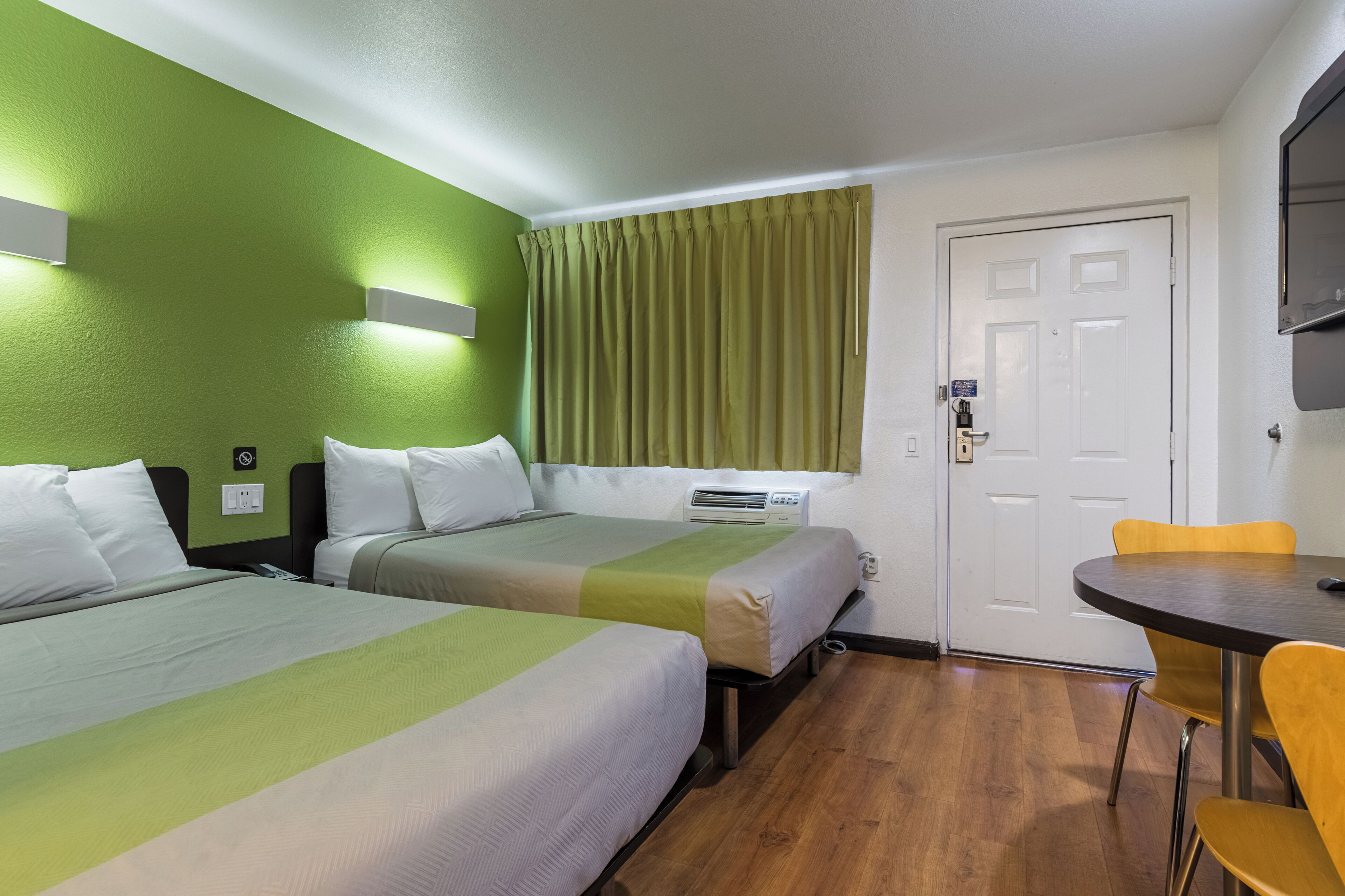 Quarto de hotel com duas camas, uma mesa de jantar e uma televisão.