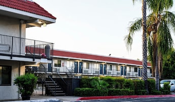 Um motel com teto vermelho, varanda no segundo andar e área de estacionamento com uma palmeira.