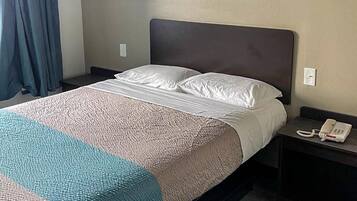 Quarto de hotel com uma cama, telefone de mesa e janela com cortinas.