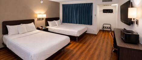 Quarto de hotel com duas camas, uma escrivaninha com cadeira, televisão e janela com cortinas.