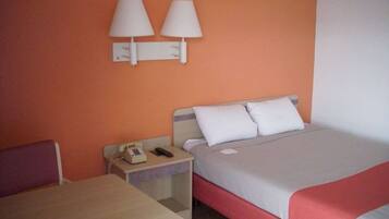 Quarto de hotel com cama, mesa de cabeceira com telefone e duas luminárias fixadas na parede.