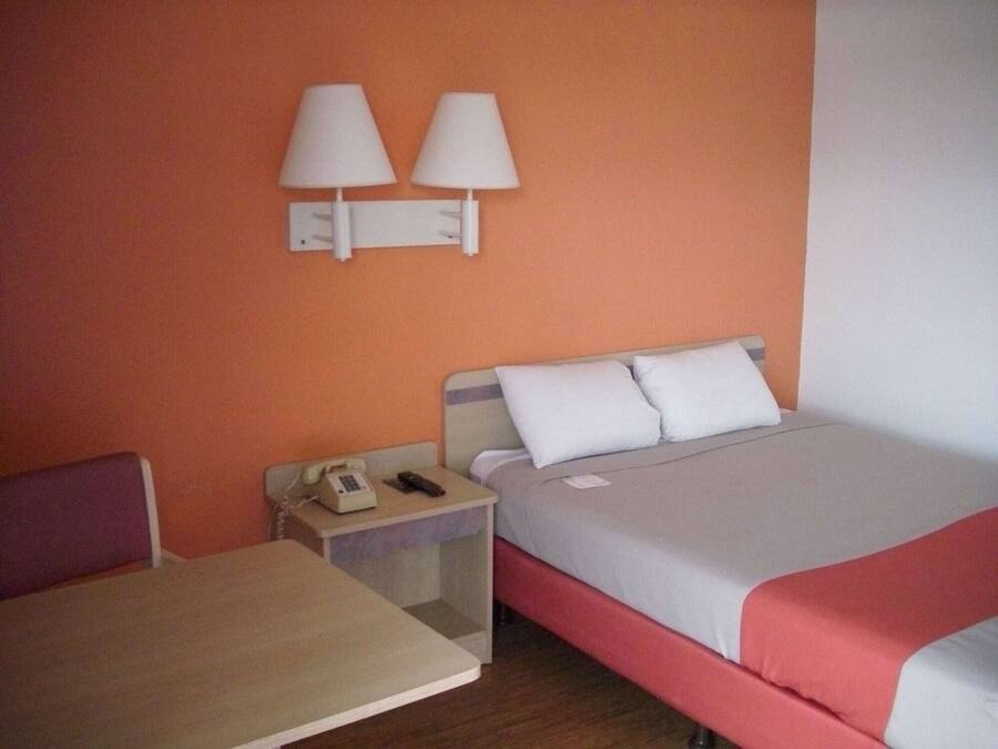 Quarto de hotel com cama, mesa de cabeceira com telefone e duas luminárias fixadas na parede.