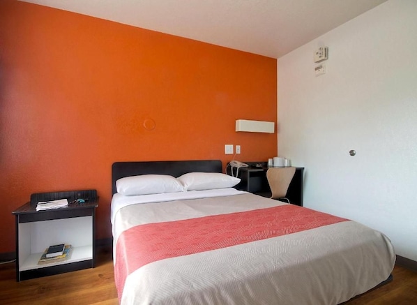 Quarto de hotel com cama, mesa de cabeceira, escrivaninha e cadeira.