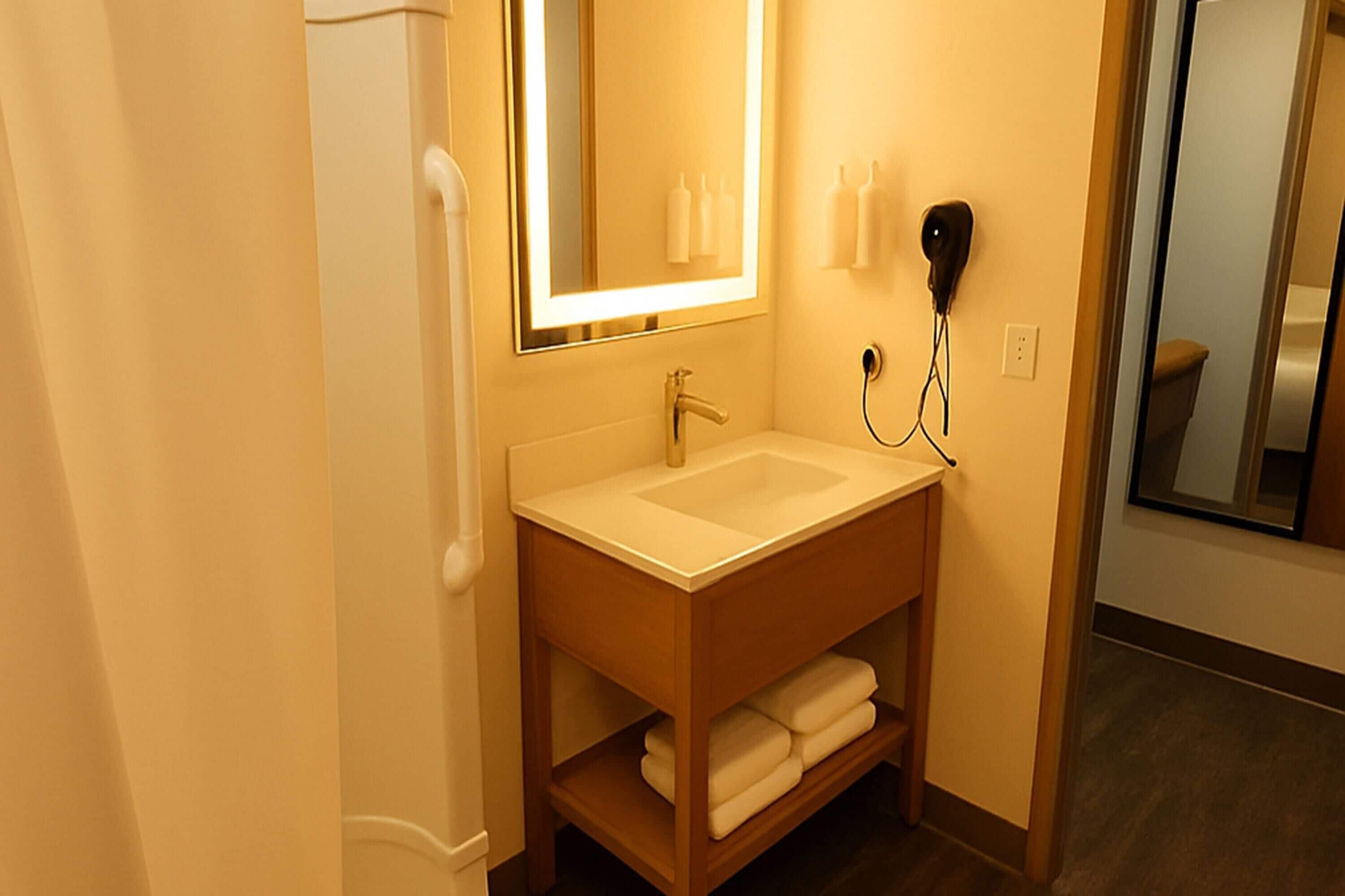 Casa de banho com lavatório, espelho, porta-toalhas e secador de cabelo.