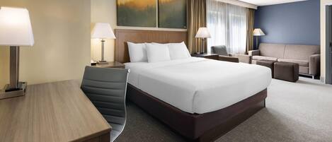 Quarto de hotel com uma cama grande, uma escrivaninha, uma cadeira, um sofá e duas luminárias.