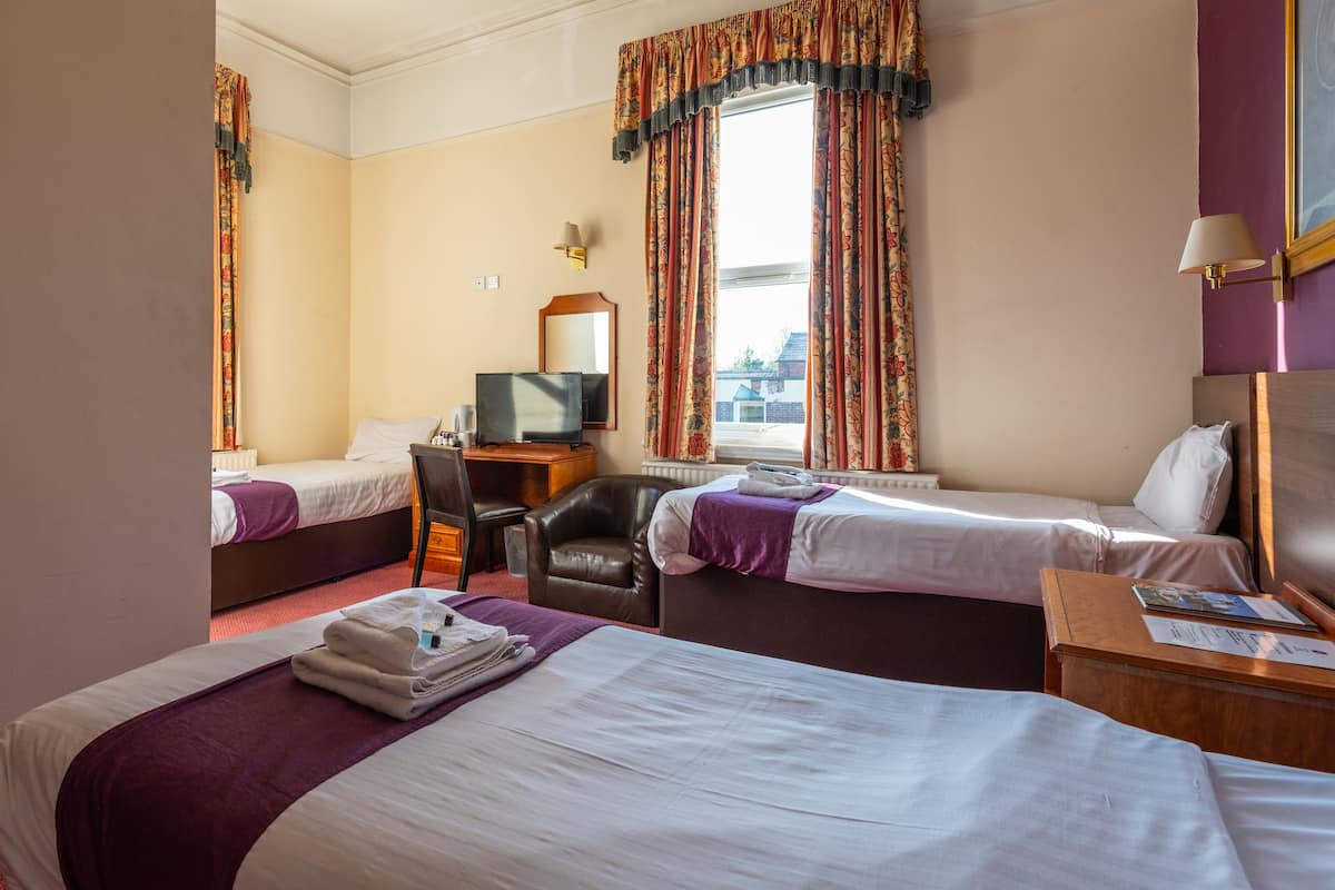 Quarto de hotel com duas camas, uma mesa com computador, uma cadeira e uma janela com cortinas.