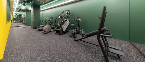 Uma academia com equipamentos de ginástica, paredes verdes e piso salpicado.