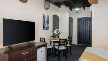 Quarto de hotel com cama, televisão em cómoda de madeira, mesa de jantar com cadeiras e um pequeno frigorífico.