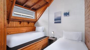 Quarto com duas camas, vigas de madeira no teto, claraboia e paredes brancas.