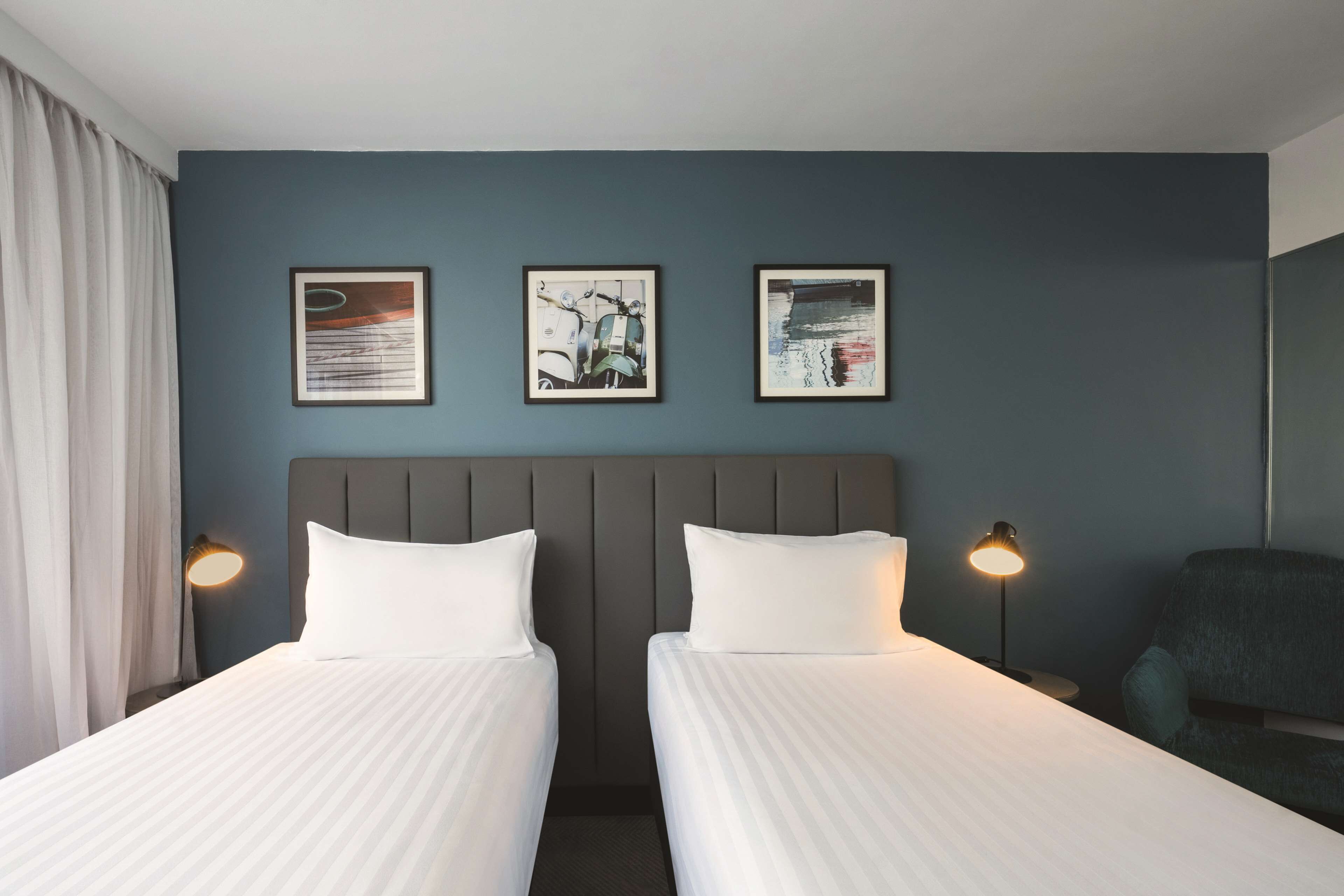Quarto de hotel com duas camas, cabeceira e três quadros na parede.