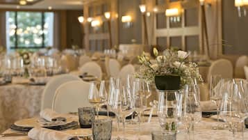Salão de banquetes com mesas montadas para um evento formal, com copos, pratos e um arranjo de flores.