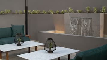 Uma área externa moderna com dois mesas de mármore branco, um sofá verde e uma parede decorativa com plantas.