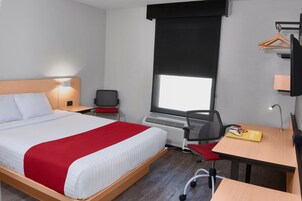Quarto de hotel com cama, escrivaninha, cadeira e janela com persiana preta.