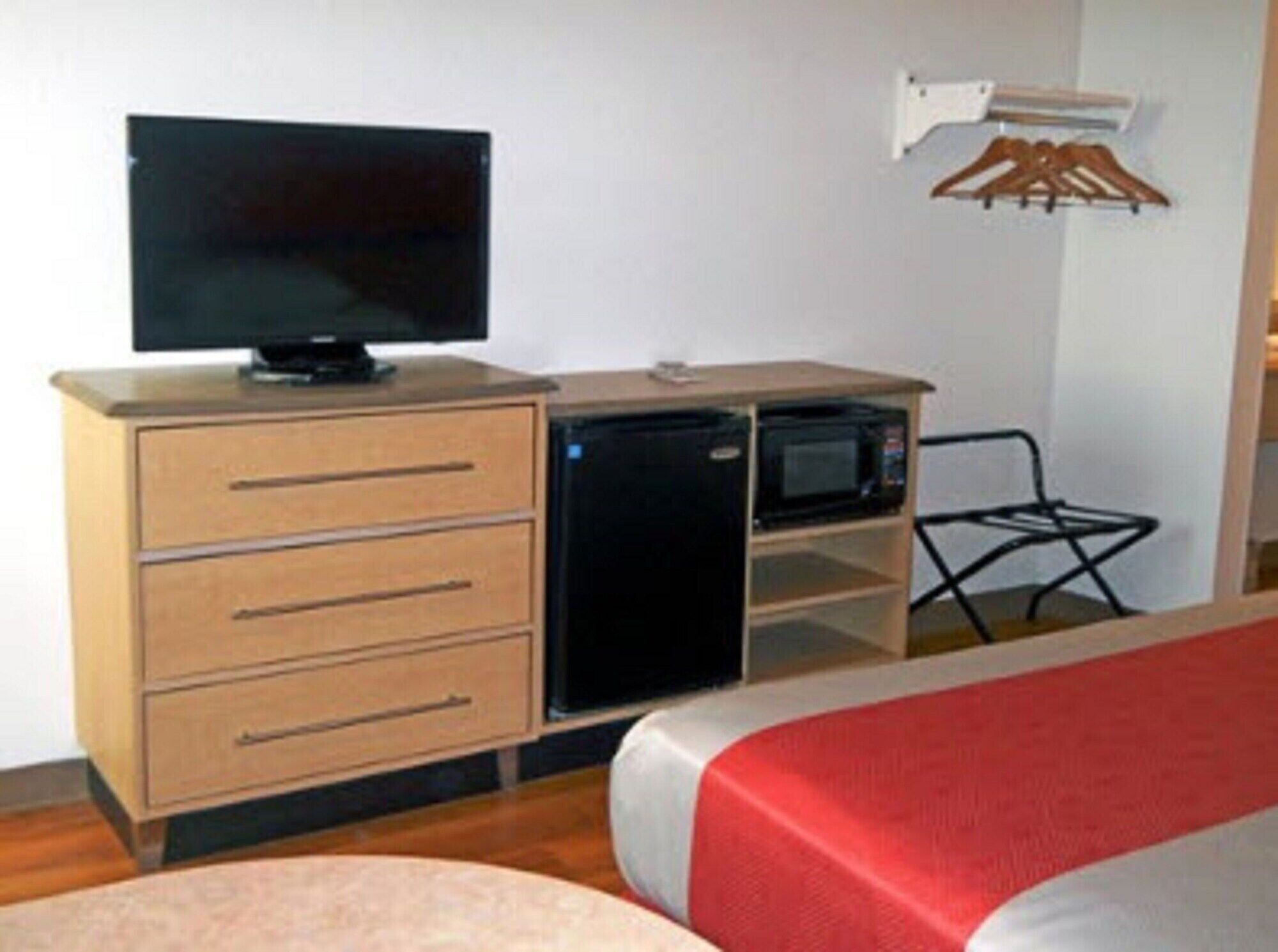 Quarto com cama, televisão sobre uma cômoda de madeira, micro-ondas e uma cadeira.