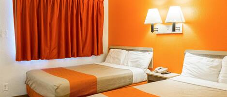 Quarto de hotel com duas camas, cortinas laranja e duas luminárias fixadas na parede.