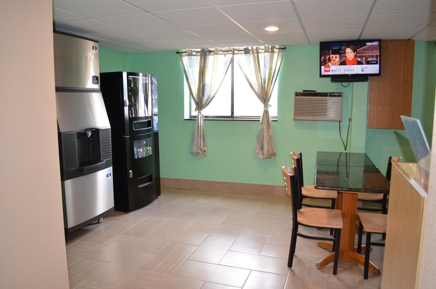 Quarto pequeno e limpo com frigorífico, micro-ondas, máquina de café, televisão e mesa de jantar com cadeiras.