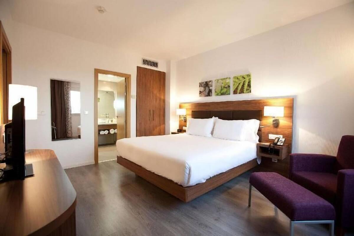 Quarto de hotel com uma cama grande, uma mesa, uma cadeira e uma televisão.