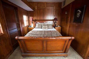 Uma cama de madeira com dossel, um encabeadura combinando, duas mesas de cabeceira com luminárias e um quadro na parede.