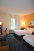 Quarto de hotel com cama, escrivaninha, cadeira, luminária e janela com cortinas.