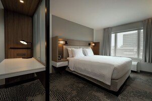 Quarto de hotel moderno com uma cama grande, mesas de cabeceira, escrivaninha e uma janela com cortinas.