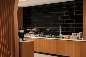 Uma cozinha moderna com painel de azulejos pretos, armários de madeira e diversos itens de café da manhã sobre a bancada.