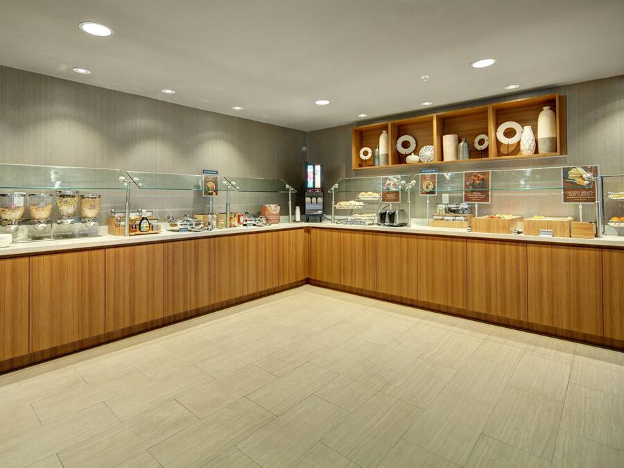 Uma área de buffet com diversos pontos de comida, incluindo uma exposição de frutas e um espaço para bebidas.