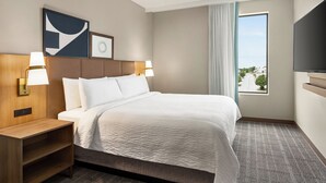 Quarto de hotel com cama, luminárias de cabeceira, TV de tela plana, janela com vista e uma obra de arte na parede.