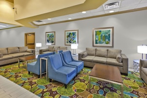 Um hall de hotel com várias áreas de estar, incluindo sofás e poltronas, e um tapete estampado.