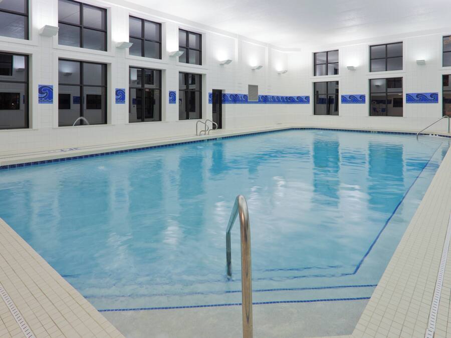 Piscina interna com água azul cristalina, rodeada por paredes de azulejos brancos com padrões decorativos azuis, e grandes janelas.