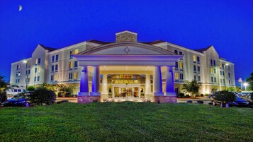 Um hotel de vários andares com uma entrada imponente, grandes colunas e um jardim frontal bem cuidado.