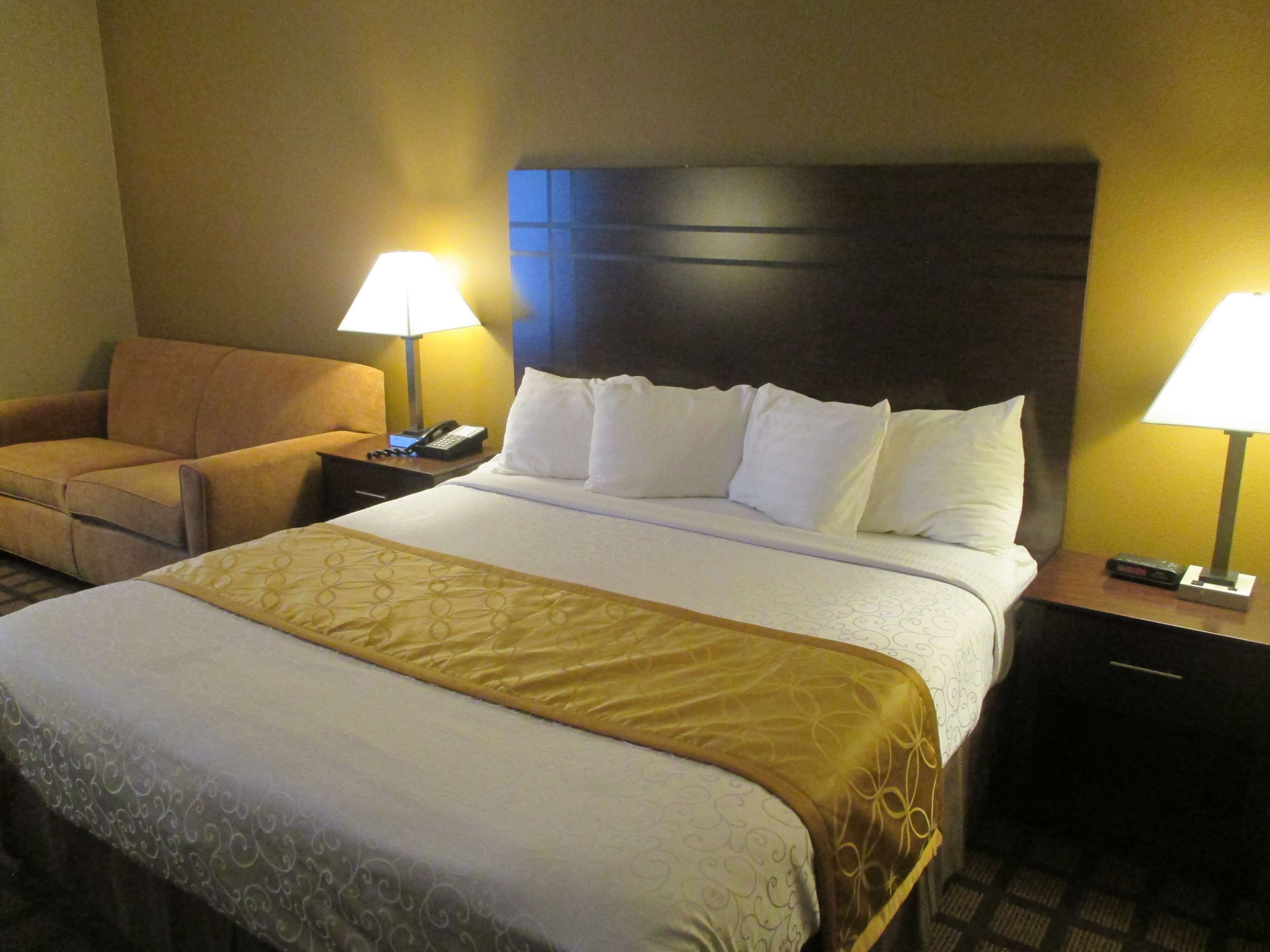 Quarto de hotel com uma cama grande, duas luminárias de cabeceira, uma cadeira e mesa de cabeceira com telefone.
