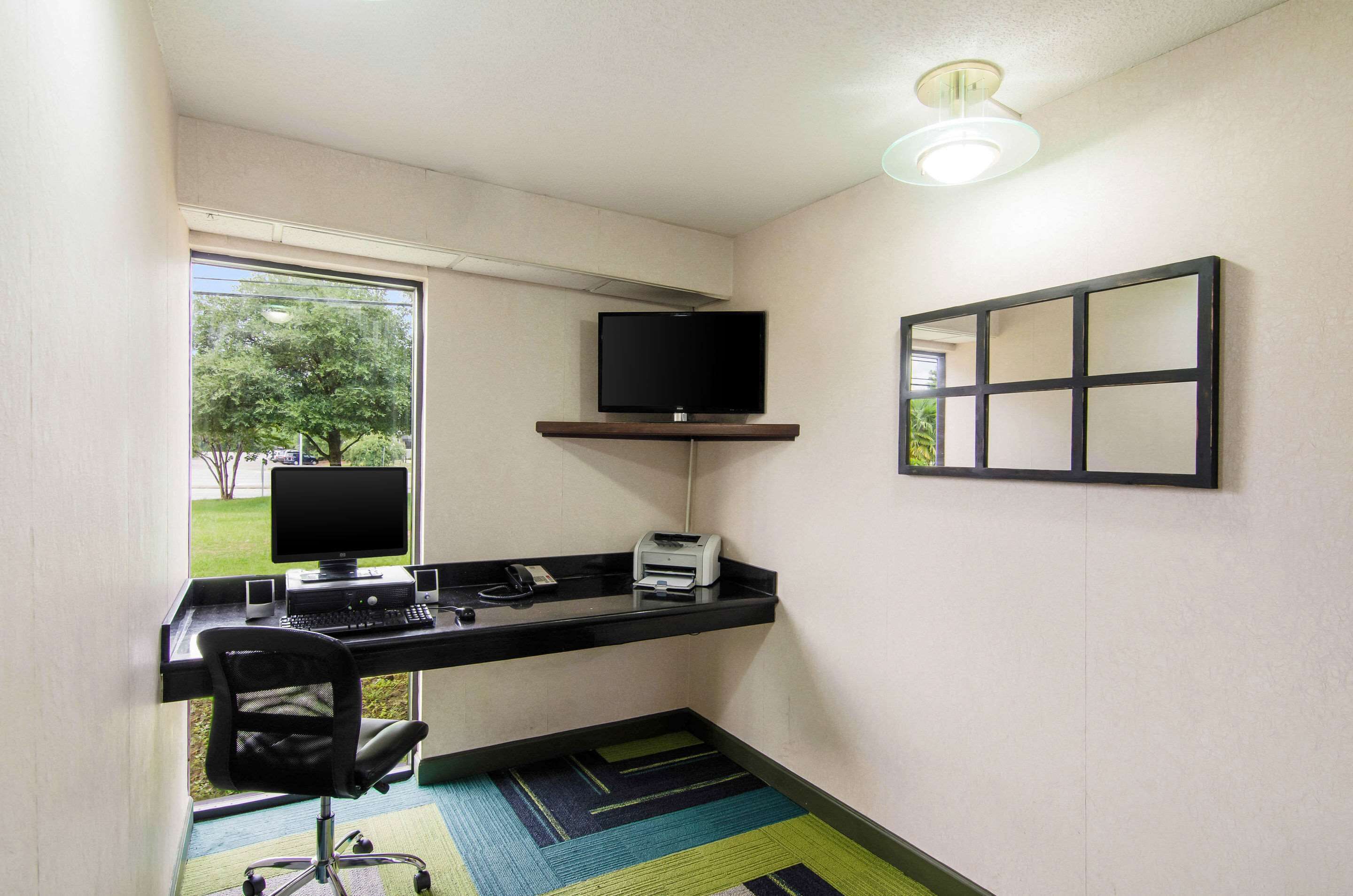 Espaço de escritório compacto com escrivaninha, cadeira, computador e uma TV fixada na parede.