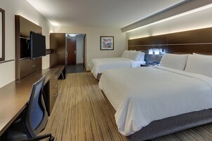 Quarto de hotel com duas camas, uma escrivaninha com cadeira, televisão e porta para um corredor.