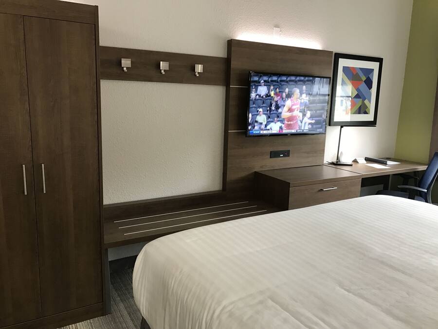 Quarto de hotel com cama, escrivaninha, televisão presa na parede, armário e quadro emoldurado.