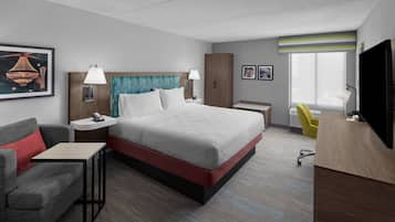 Quarto de hotel com cama, escrivaninha, cadeira, televisão e obras de arte nas paredes.