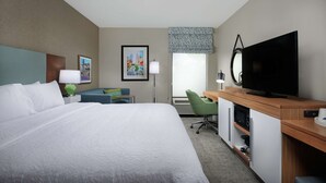 Quarto de hotel com uma cama grande, uma escrivaninha com computador, televisão e janela com vista.