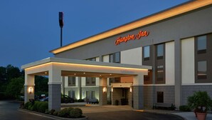 Entrada de um hotel Hampton Inn, com área externa coberta, uma placa de identificação e estacionamento.