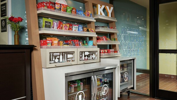 Uma área com máquinas de venda automática, com lanches e bebidas, um aviso com 'KY' e uma mensagem na parede.