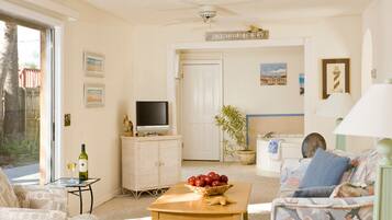 Sala de estar com televisão, mesa de jantar com frutas, sofá e vista para o exterior.