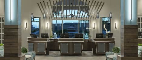 Uma área de recepção com design moderno, destacando um balcão central com dois laptops, cercado por cadeiras estampadas e uma grande janela com vista para edifícios.