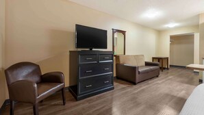 Quarto de hotel com televisão de tela plana em uma cômoda, uma poltrona de couro, um sofá e uma pequena mesa.