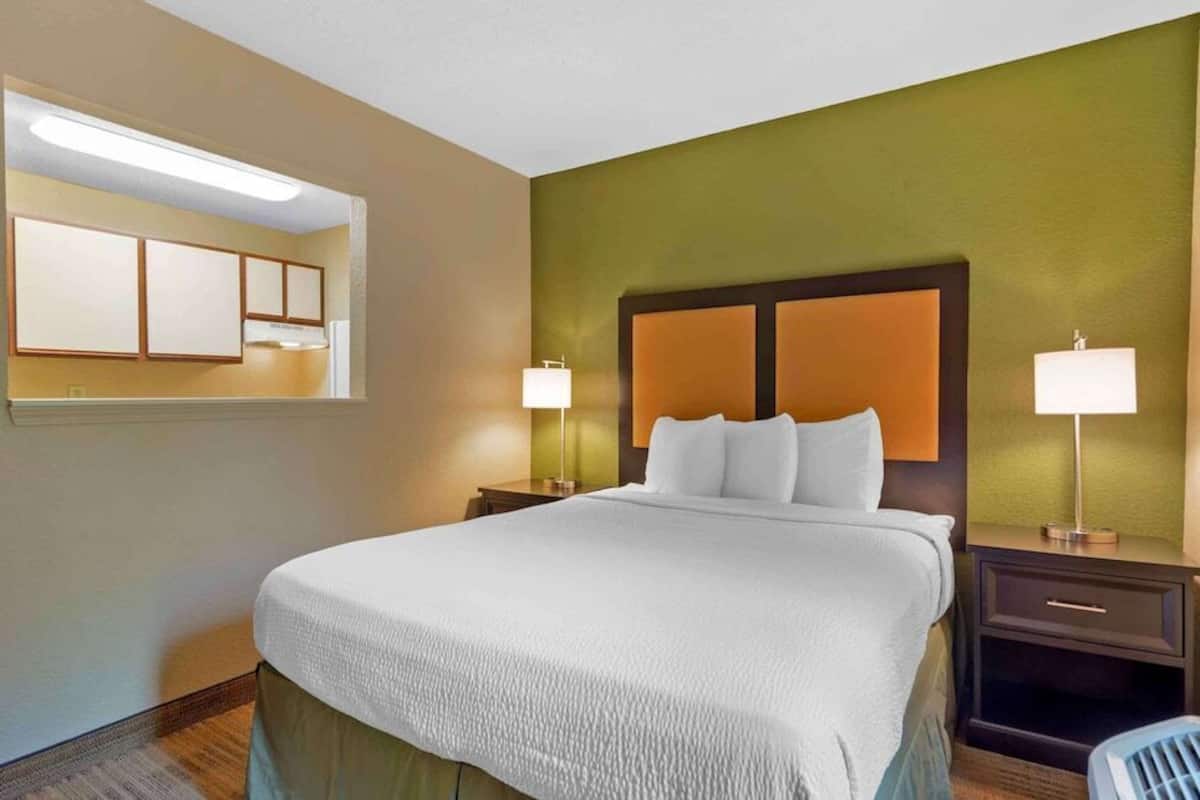 Quarto de hotel com cama, mesas de cabeceira, espelho e janela.