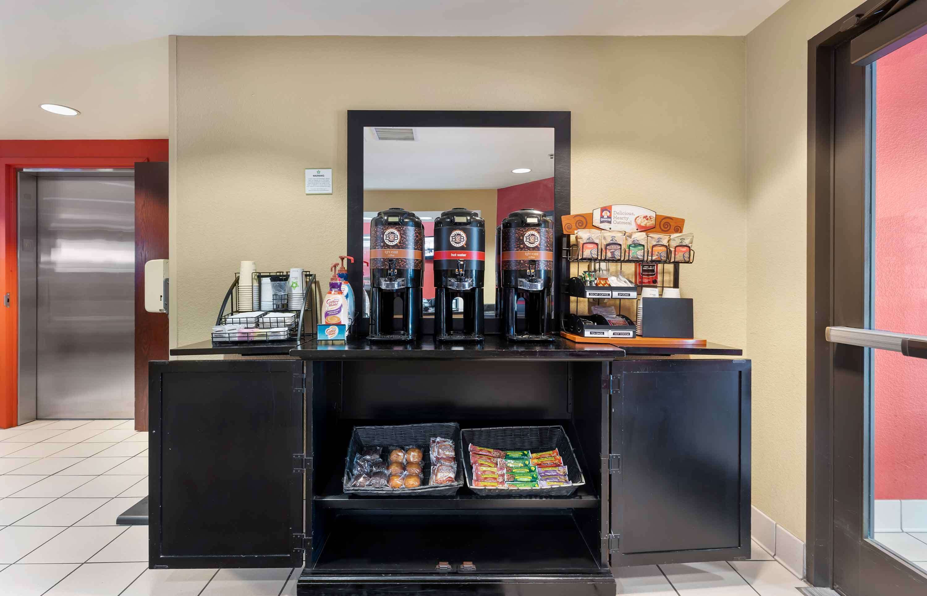 Uma estação de café com vários distribuidores, um refrigerador e recipientes para lanches.