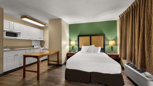 Quarto de hotel com cozinha compacta, cama, escrivaninha e mesa de cabeceira.