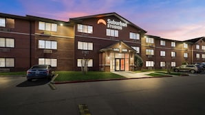 Um hotel Suburban Studios com fachada de tijolos, diversas janelas e entrada bem iluminada.