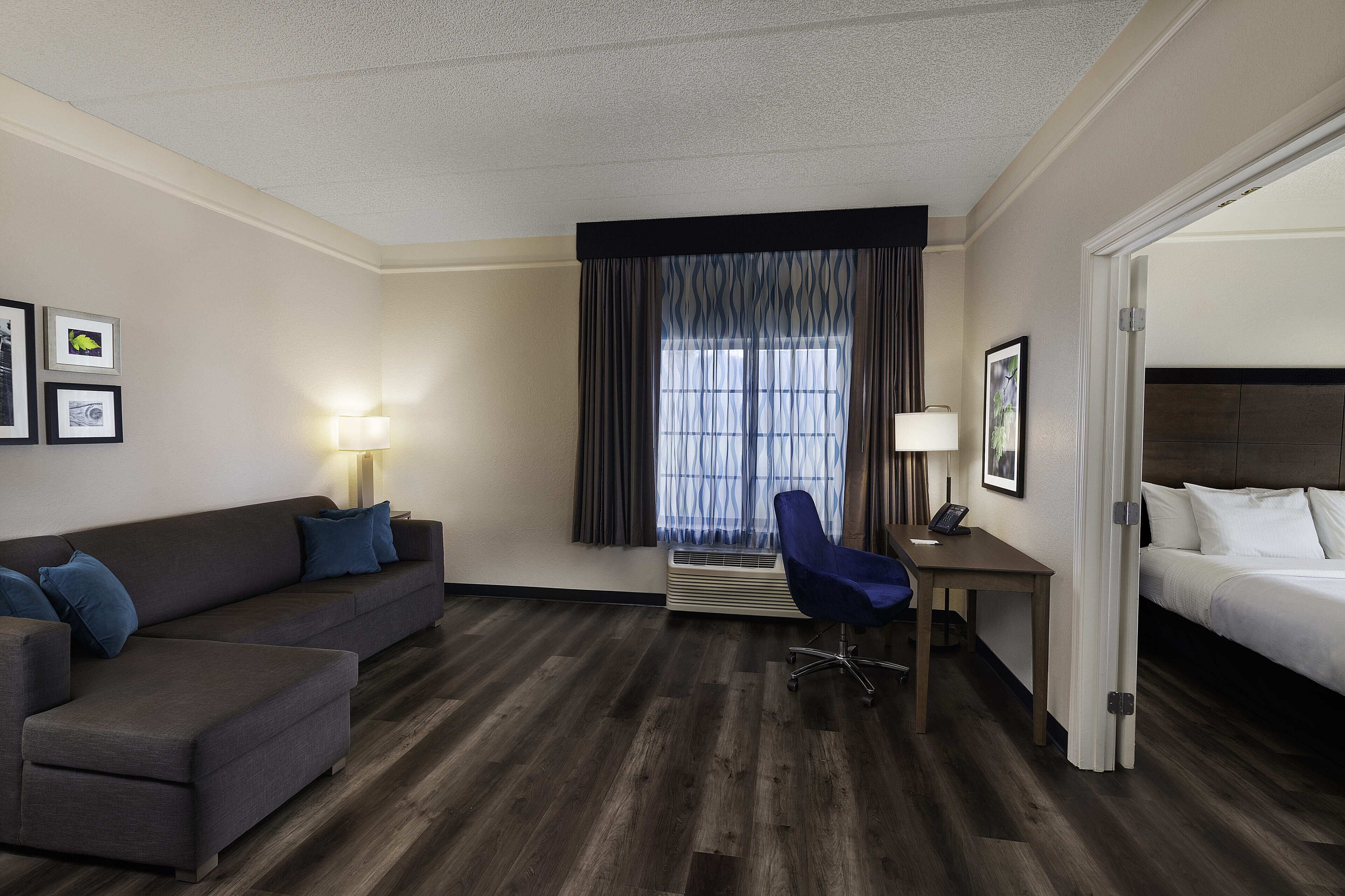 Quarto de hotel com sofá, mesa de trabalho, cadeira, cama e janela com cortinas.