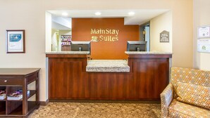 Uma receção com o letreiro 'MainStay Suites', um sofá estampado e um cartaz informativo emoldurado na parede.