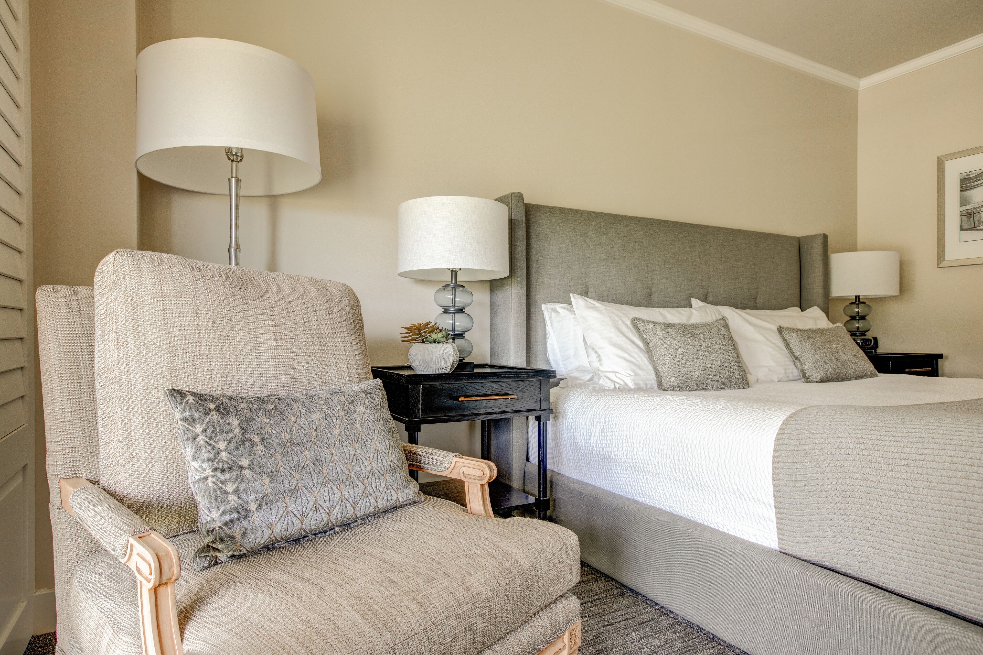 Quarto de hotel com cama, uma cadeira, mesa de cabeceira e duas luminárias.